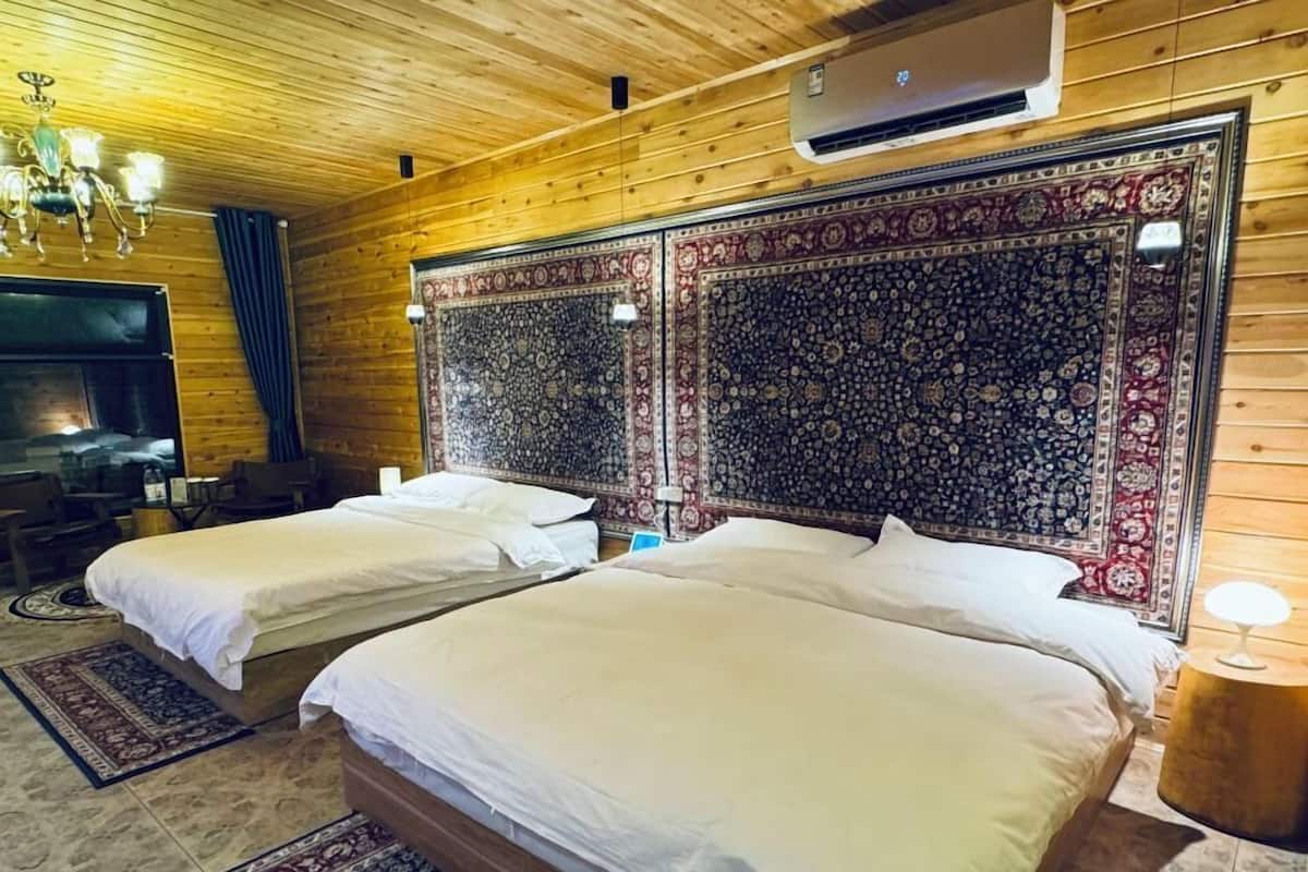 Quarto com duas camas, paredes de madeira, um candelabro e um grande tapeçar com padrão.