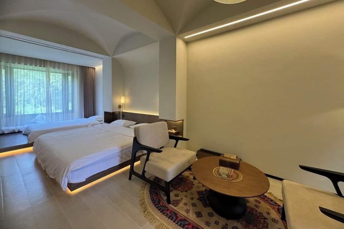 Quarto de hotel moderno com uma cama grande, uma mesa de centro redonda e um espaço de estar.