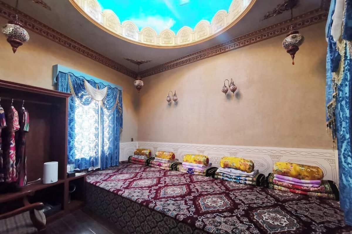 Quarto com carpete estampado, cama com várias almofadas, guarda-roupa e luminária decorativa no teto.