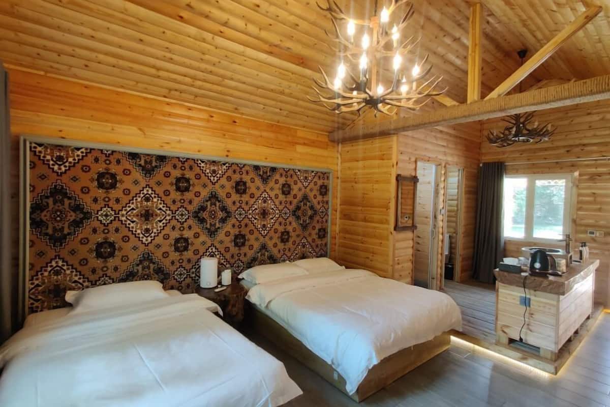 Uma cabana de madeira com duas camas, um painel de cabeceira estampado, um candelabro e uma área de cozinha.