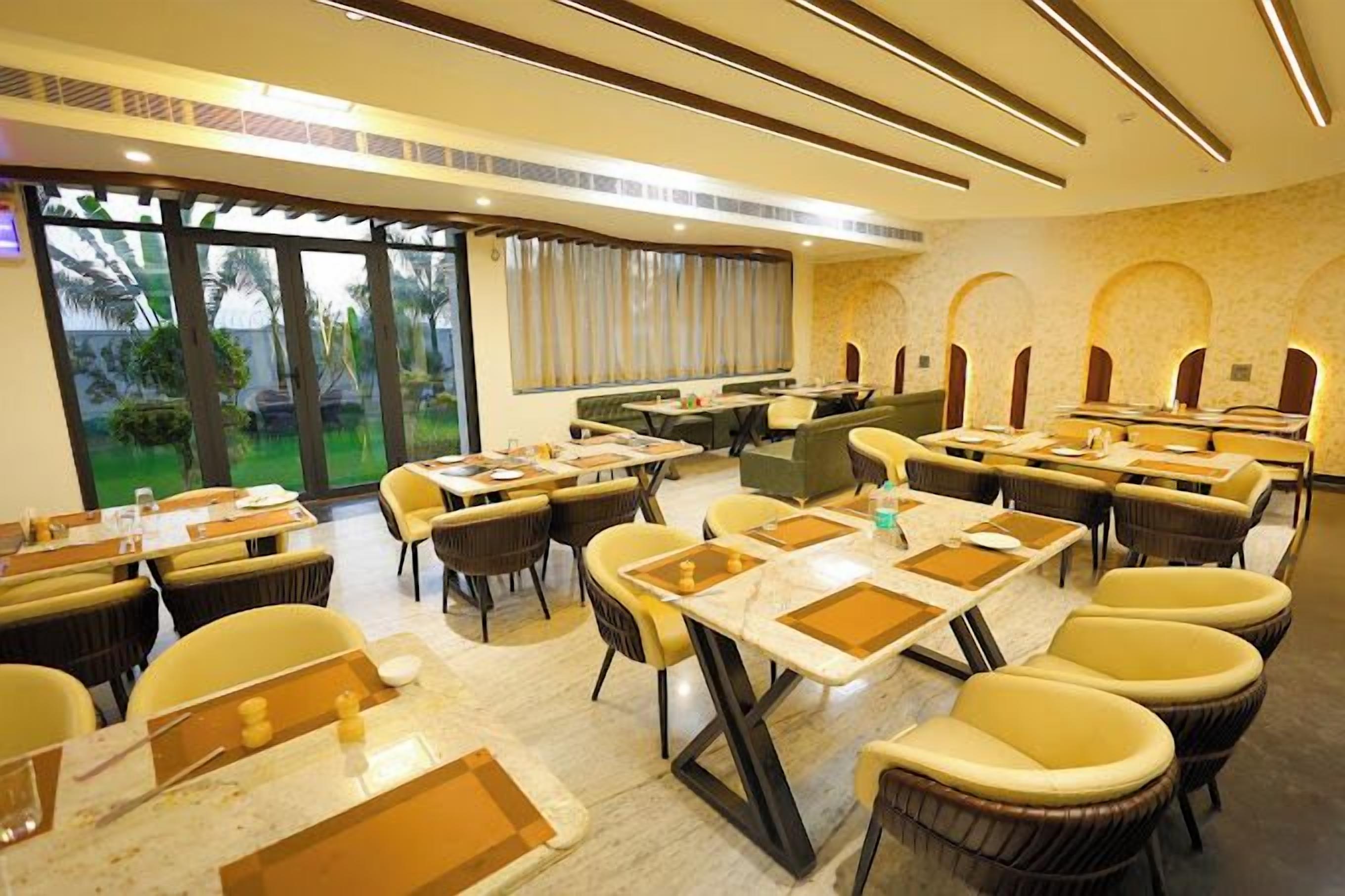 Um restaurante espaçoso com tetos altos, iluminação moderna e grandes janelas que oferecem vista para o verde.