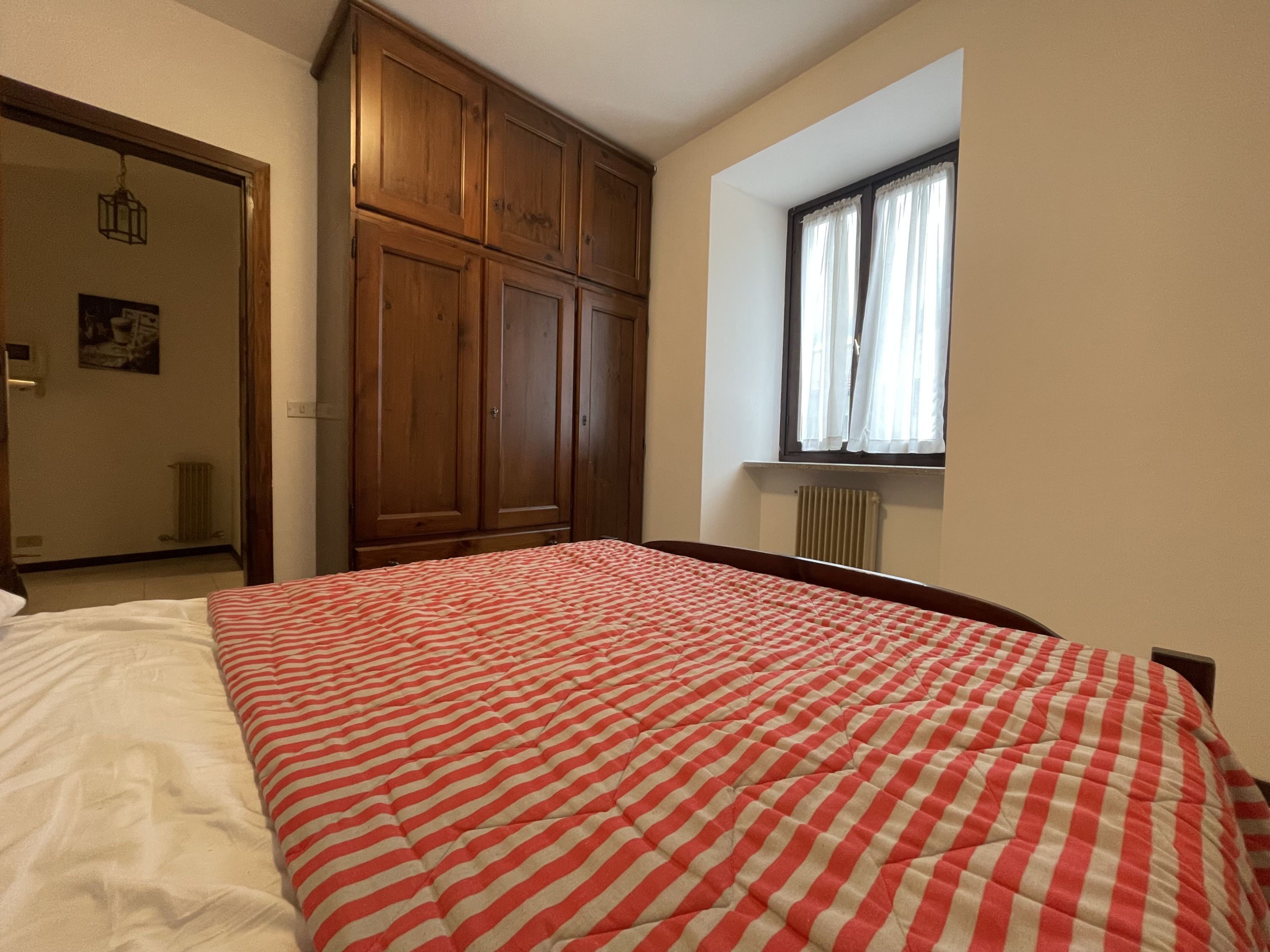 Quarto com cama, guarda-roupa de madeira e janela com cortinas.