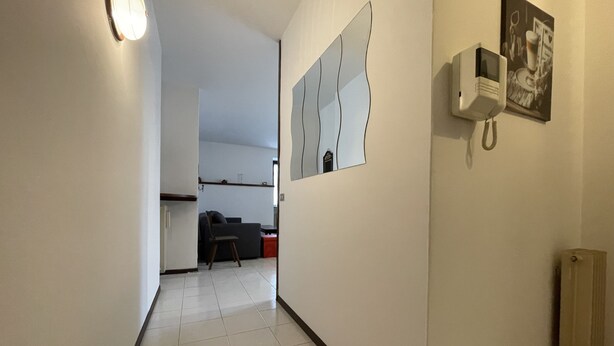Um corredor com piso de azulejos, telefone fixado na parede e quadro emoldurado.
