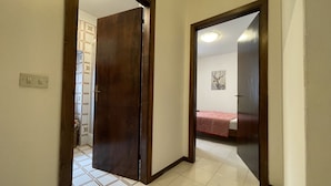 Um corredor com chão em mosaico que leva a um quarto com cama e um quadro na parede.