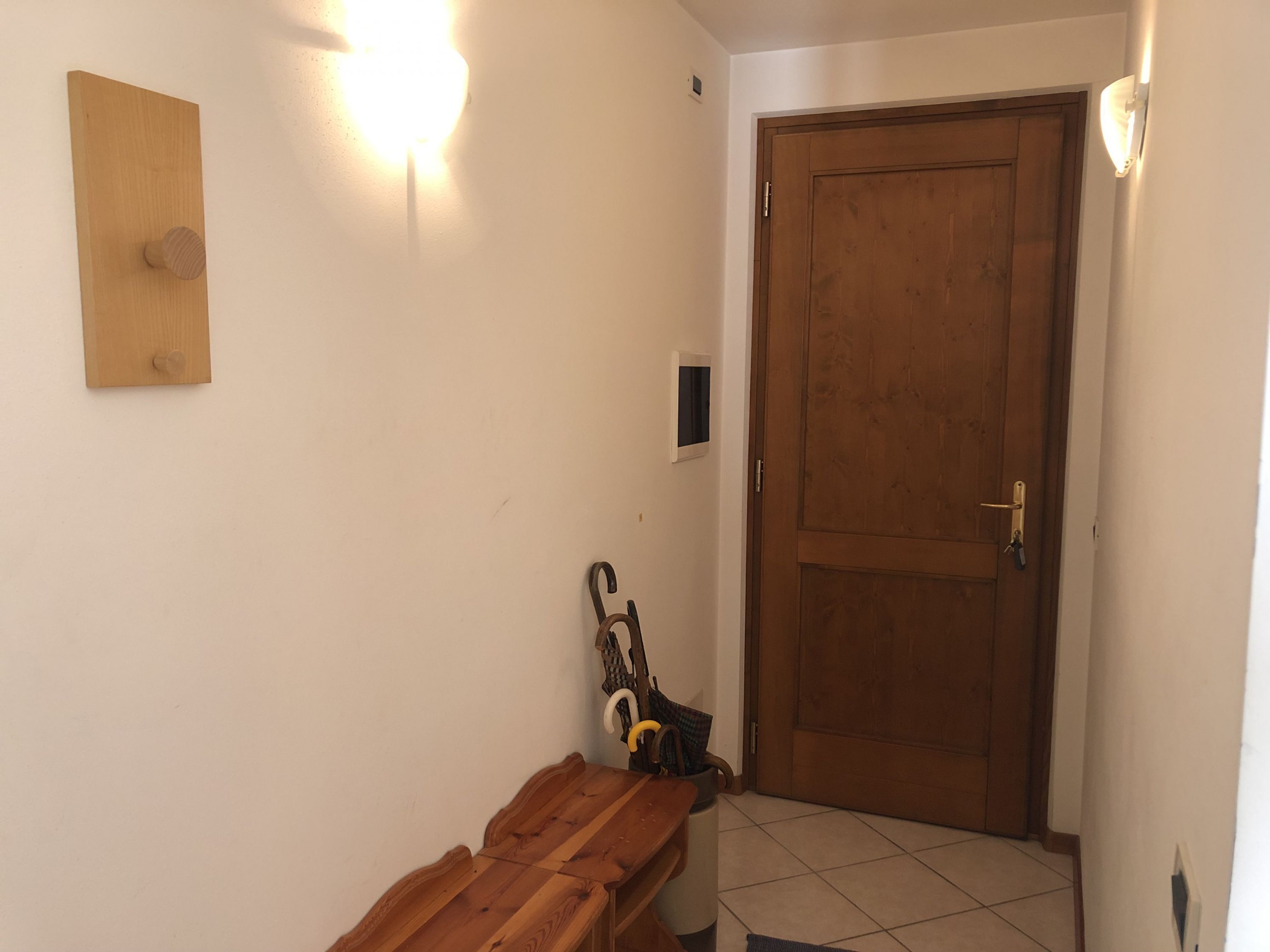 Um corredor com um banco de madeira, uma porta e luminárias na parede.