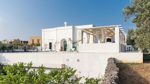 Um edifício moderno branco com terraço no telhado, pérgola e uma parede de pedra.