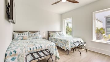 Quarto com duas camas, ventoinha no teto e uma janela grande com vista para edifícios e palmeiras.