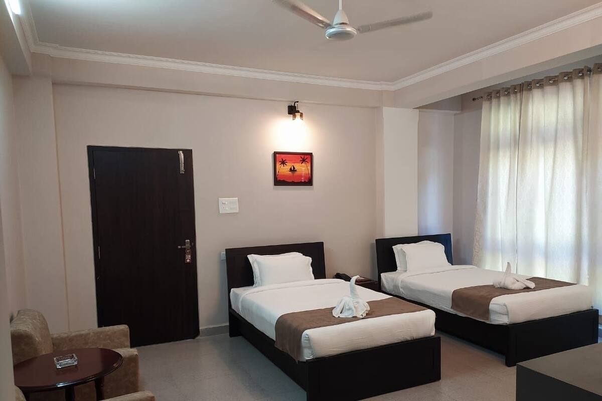 Quarto de hotel com duas camas, uma escrivaninha, uma cadeira, uma porta e um quadro na parede.