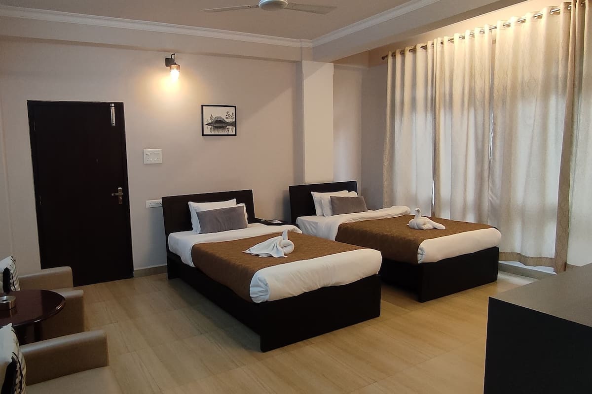 Quarto de hotel com duas camas, uma escrivaninha, uma cadeira e um ventilador de teto.