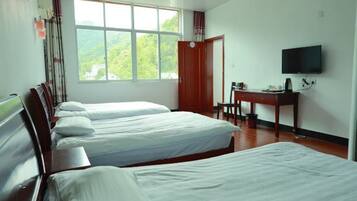 Quarto de hotel com duas camas, uma escrivaninha, uma cadeira, televisão e janela com vista para o verde.