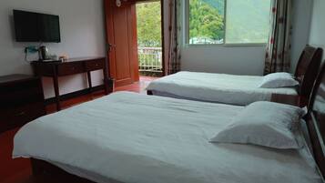 Quarto de hotel com duas camas, televisão, escrivaninha e varanda com vista para as montanhas.