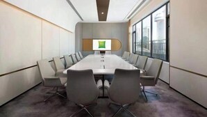 Sala de conferência com uma mesa comprida, várias cadeiras, um ecrã grande e janelas amplas.