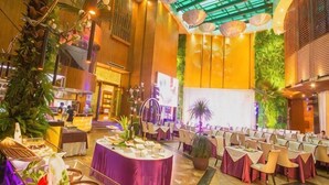 Um espaço amplo e interno com mesas redondas, cadeiras e um palco.
