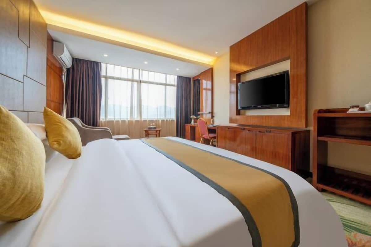 Quarto de hotel com uma cama grande, uma escrivaninha, uma cadeira, uma televisão e uma janela com cortinas.