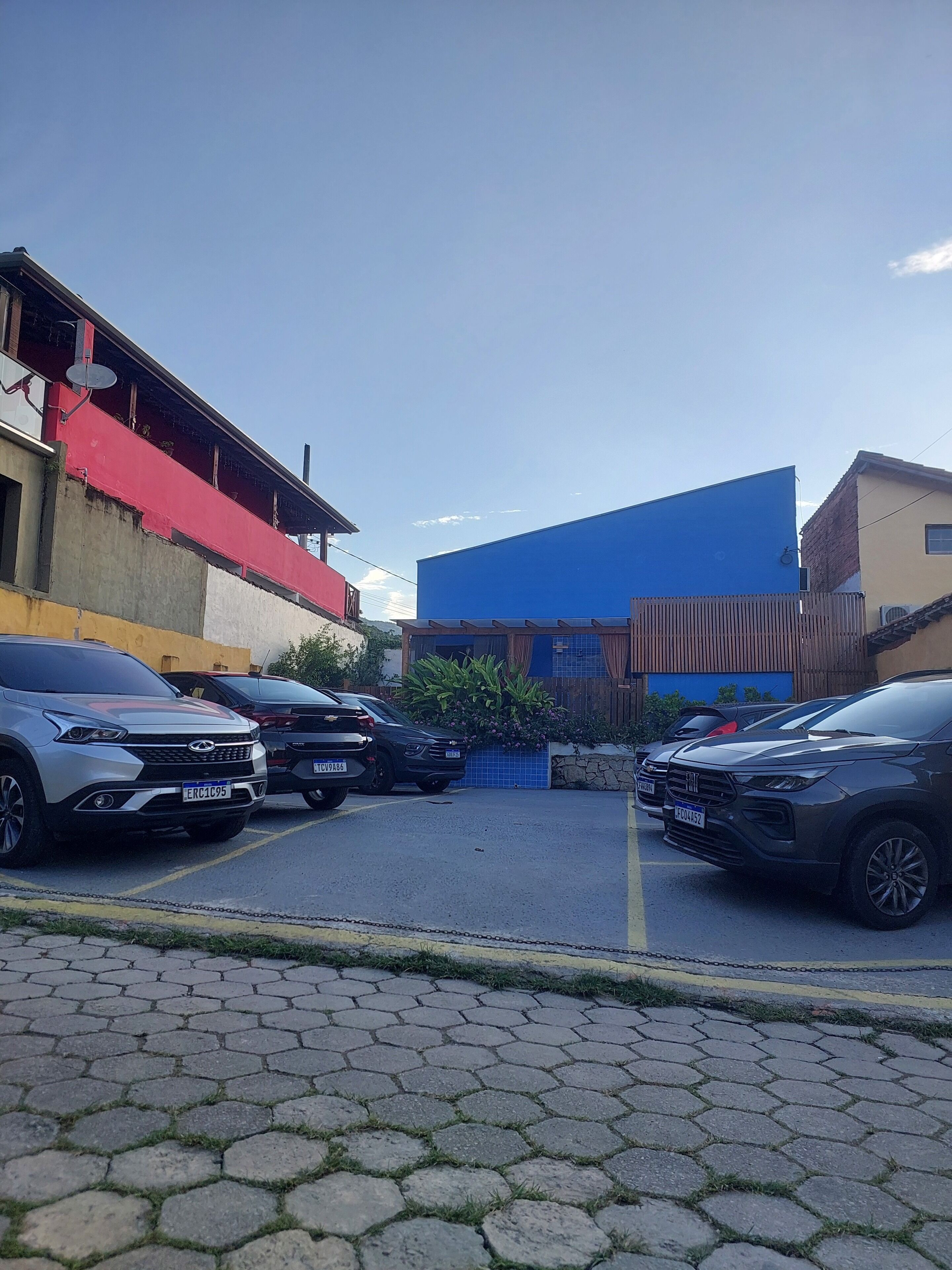 Um estacionamento com vários carros, um edifício com fachada azul e uma construção com telhado vermelho.