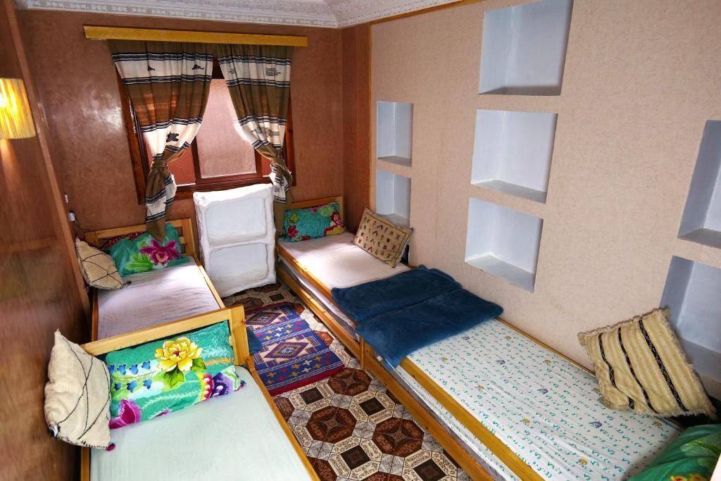 Quarto compacto com duas camas, uma mesinha e uma cadeira.