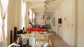 Uma sala de jantar espaçosa com uma mesa comprida e cadeiras, um ventilador de teto e uma cozinha ao fundo.