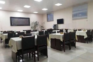 Sala de conferências com mesas, cadeiras, uma tela grande e uma planta.