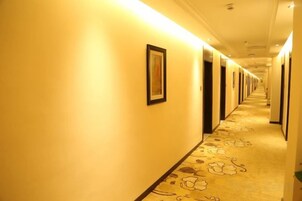 Corredor de hotel com portas em ambos os lados, carpete com padrão floral e um quadro na parede.