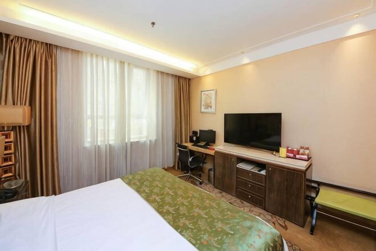 Quarto de hotel com cama, escrivaninha, televisão e janela com cortinas.