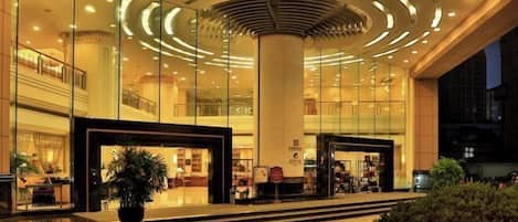 Um saguão de hotel moderno com uma coluna central, portas de vidro e um design de teto circular.