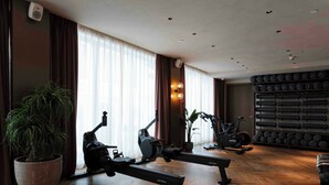 Uma academia com bicicletas ergométricas, um remo e um painel de halteres.