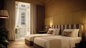 Quarto de hotel com duas camas, uma mesinha de cabeceira, um abajur, uma cadeira e vista para um edifício pela janela.