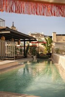 Uma área de piscina com pergolado, guarda-sóis e plantas em vasos.