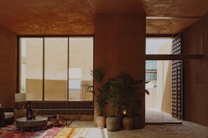 Quarto com uma janela grande, piso de madeira, sofá, mesa de centro e várias plantas em vasos.