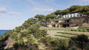 Uma villa costeira com fachada de pedra, jardins em terraços e vista para o mar.