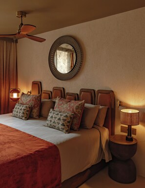 Quarto de hotel com cama, espelho redondo, ventoinha no teto e abajur.