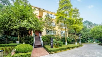 Edifício com escadaria que leva à entrada, cercado por vegetação e área pavimentada.