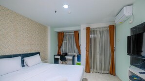 Quarto de hotel com cama, escrivaninha, cadeira, televisão e ar condicionado.