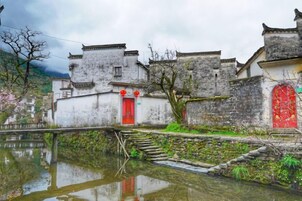 Um edifício tradicional com porta vermelha, parede de pedra e uma pequena ponte sobre a água.