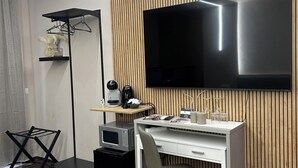 Quarto de hotel moderno com televisão de tela plana, uma escrivaninha com cadeira, micro-ondas e um cabideiro.