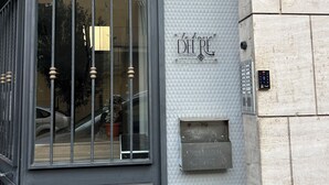 Um edifício com uma janela grande, uma porta com portão de metal e um muro com padrão geométrico e uma caixa de correio.