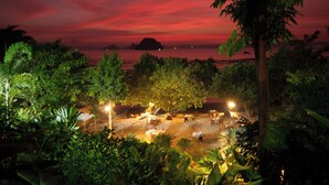 Restaurante à beira-mar com mesas ao ar livre, com vista para o mar e um pôr do sol.