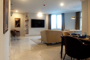 Uma sala de estar moderna com televisão de tela plana, sofá, mesa de jantar com cadeiras e uma grande janela com cortinas.