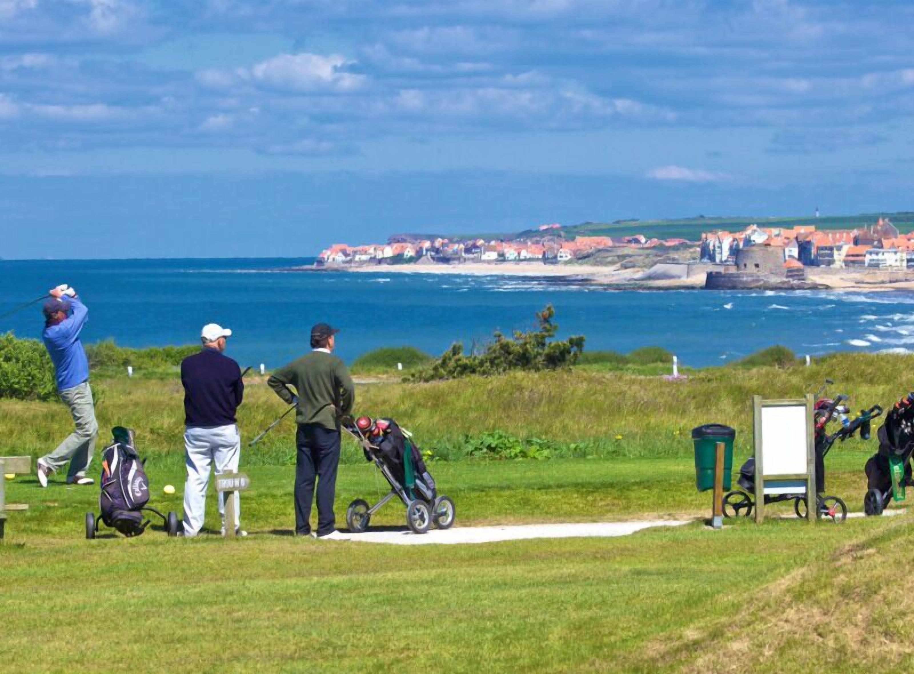 Um campo de golfe com vista para o litoral, um bunker de areia e uma haste de sinalização.