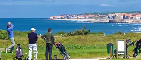 Um campo de golfe com vista para o litoral, um bunker de areia e uma haste de sinalização.