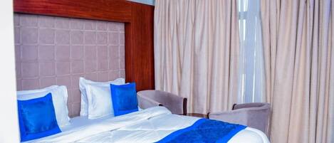 Quarto de hotel com cama, duas cadeiras, janela com cortinas e ar condicionado.