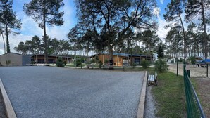 Um camping com área de estacionamento de cascalho, mesas de piquenique e um edifício com fachada de madeira.