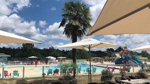 Área de piscina externa com espreguiçadeiras, guarda-sóis e um tobogã.