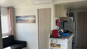 Uma cozinha compacta com micro-ondas, fogão e armários. Há uma área de refeições com uma mesa posta para dois, e um sofá em uma sala de estar adjacente.