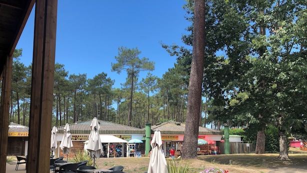 Uma área externa com mesas e cadeiras, cercada por árvores e um edifício com placas.