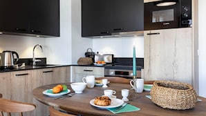 Cozinha moderna com armários escuros, uma mesa de jantar redonda com cadeiras e um micro-ondas sobre a bancada.