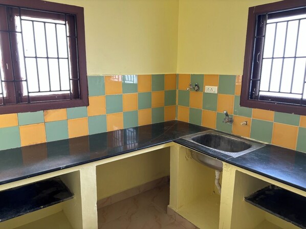 Cozinha com bancada preta, pia e janela com grades.