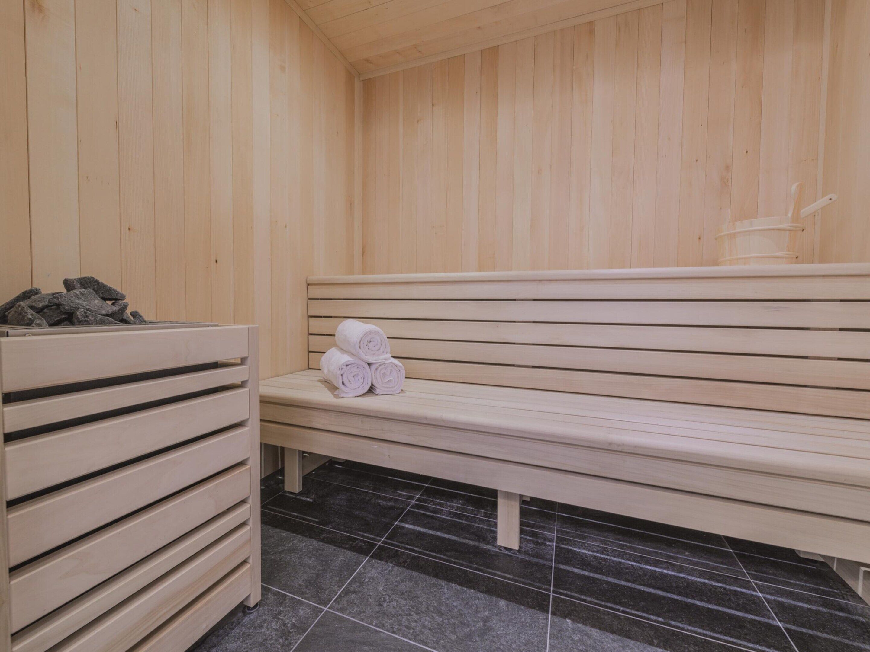 Uma sala de sauna com um banco de madeira, toalhas e um compartimento com pedras.