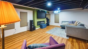 Uma sala de estar moderna com uma televisão de tela plana, um sofá, uma poltrona roxa e piso de madeira.