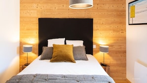 Quarto moderno com painel de parede de madeira, cabeceira preta e duas luminárias de apoio.